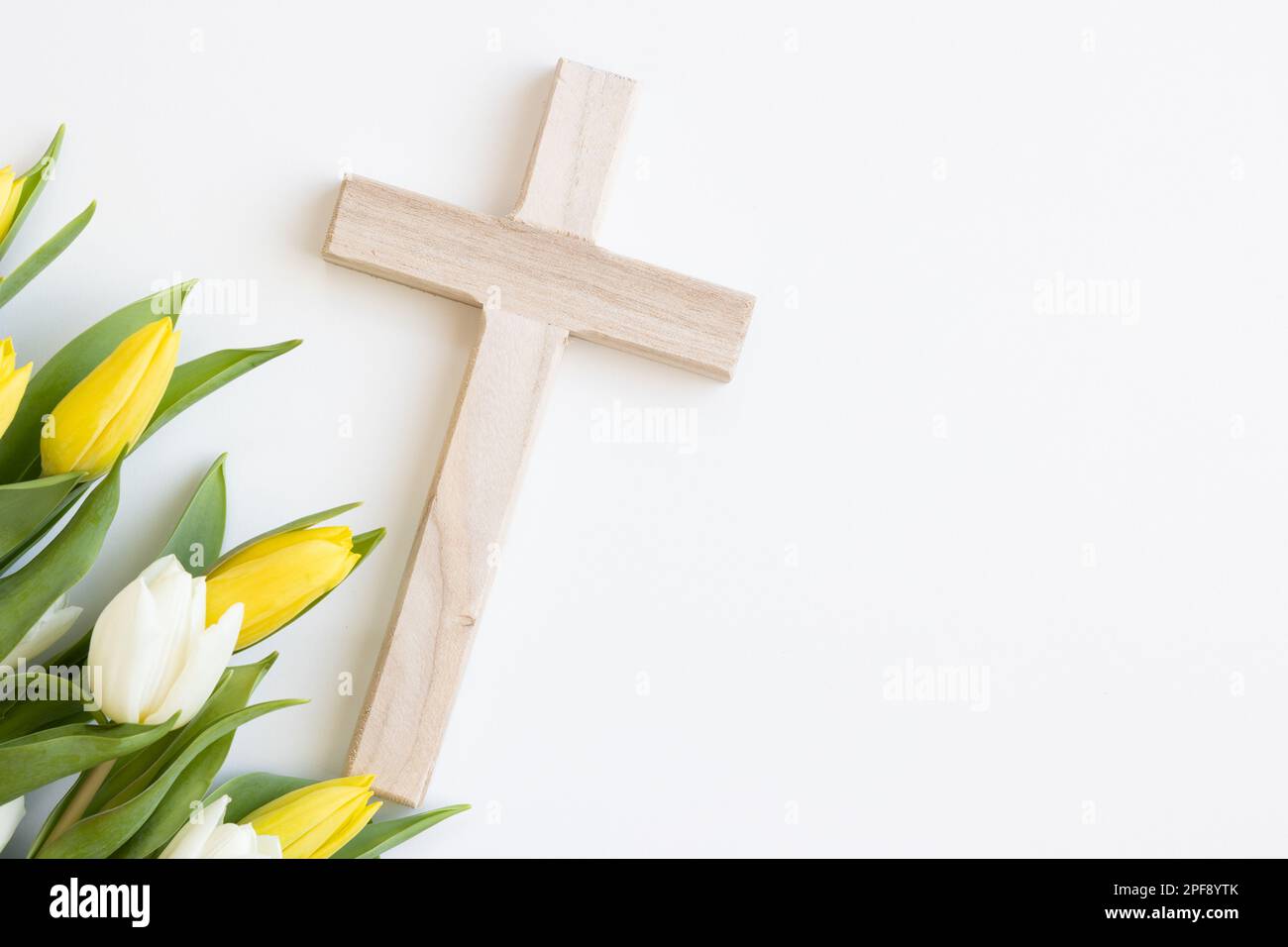 Simple wood Christian cross with yellow and white tulips on a white ...