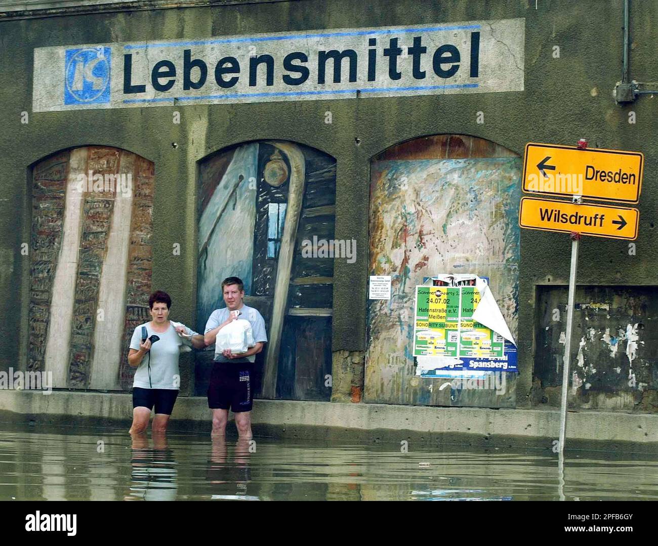 People stand in front of a former food store in the flooded city of ...