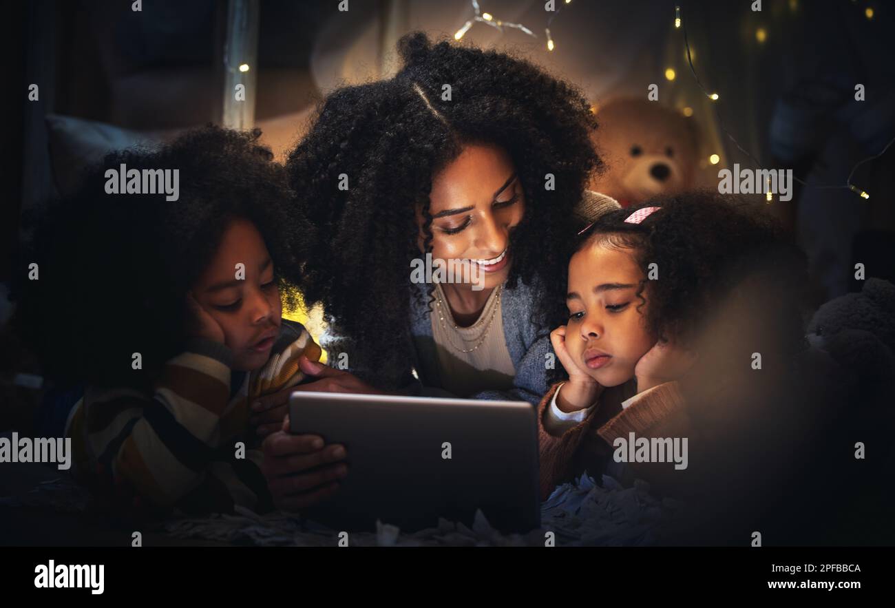 Tablet, night a mother reading to her children in a tent while camping ...