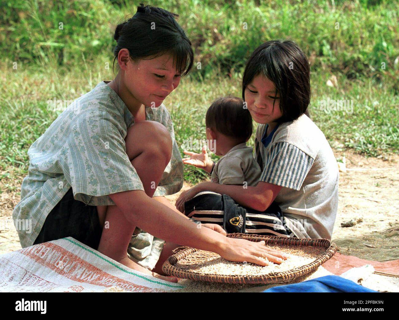 A Penan woman sorts through rice with her children at Patik village ...