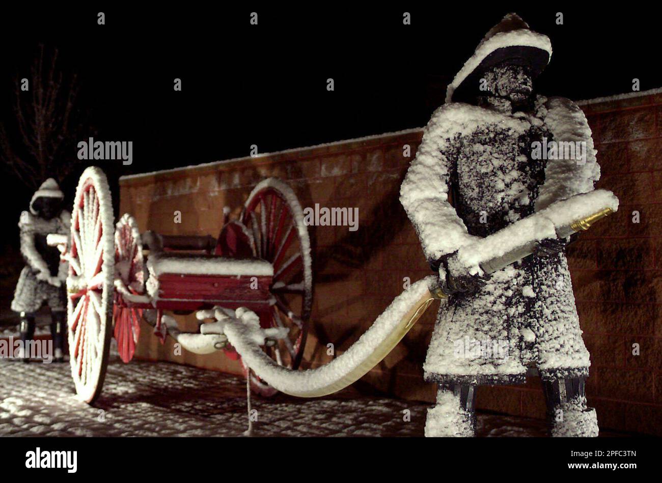 Snow collects on a sculpture of old fashioned firefighters in front of ...