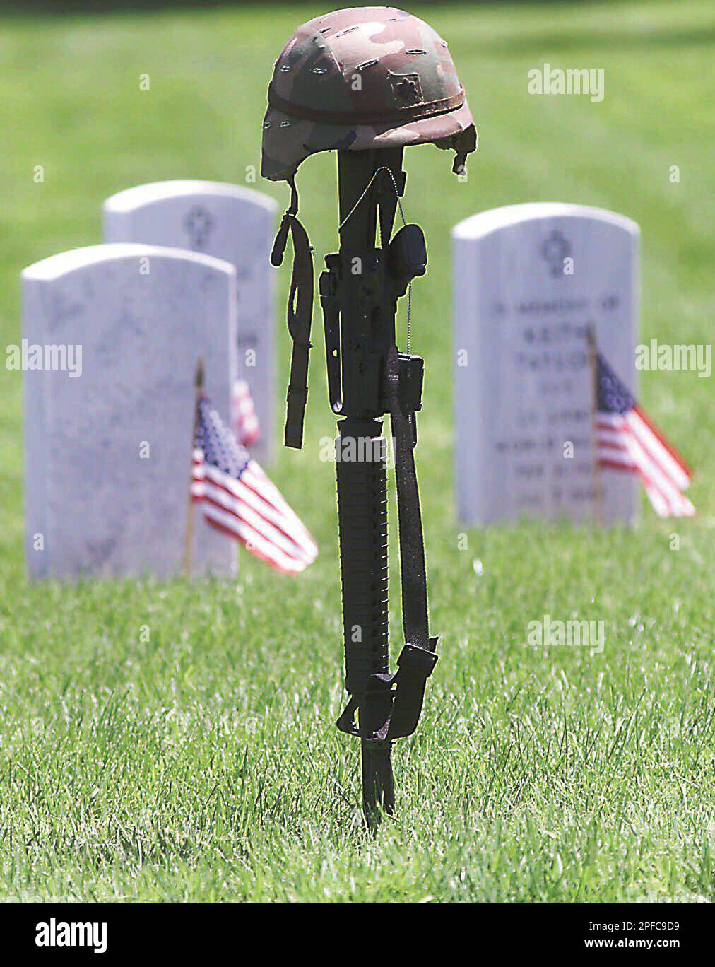 A rifle with its bayonet buried in the ground and a soldiers helmet and ...