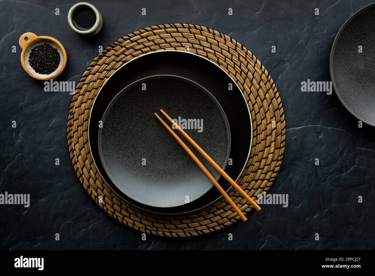 A table setting on a straw mat, with chopsticks, soya sauce and sesame ...