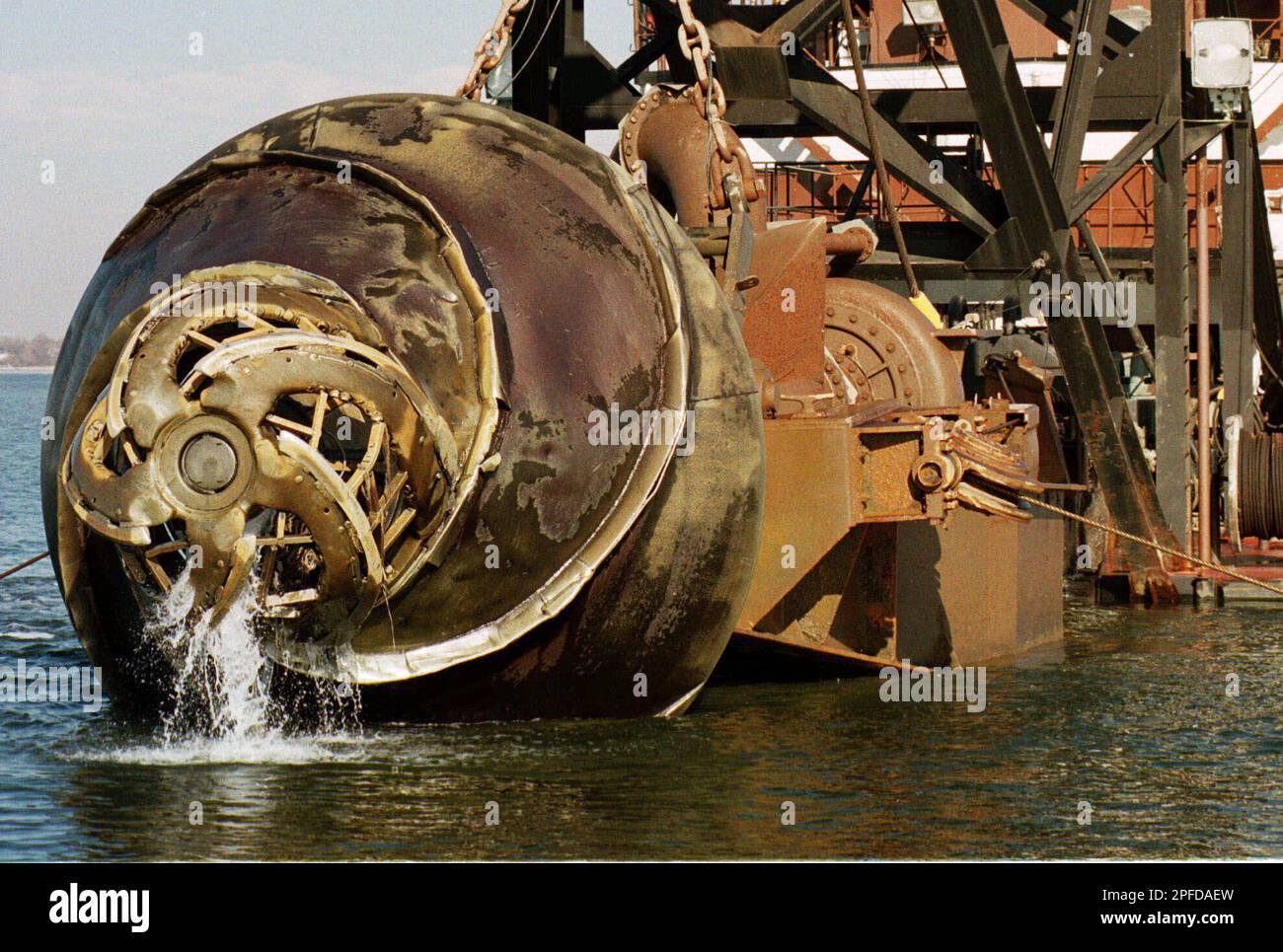 The drilling end of a river dredging barge is raised out of the water ...
