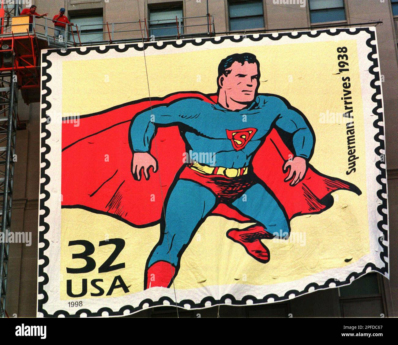 Workers raise a five-story replica of a stamp of Superman on the ...