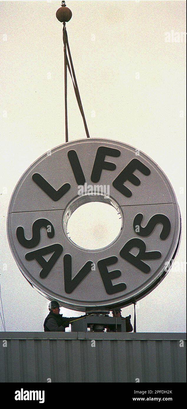 A worker guides a 12-foot Life Savers sign into place on top of the ...