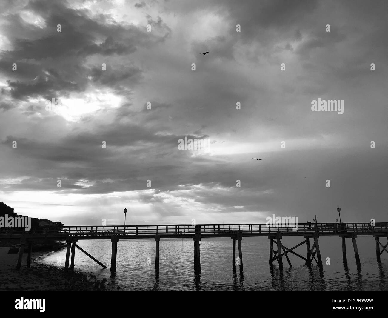 A scenic landscape of a bridge, beach, and cloudy sky over the horizon ...
