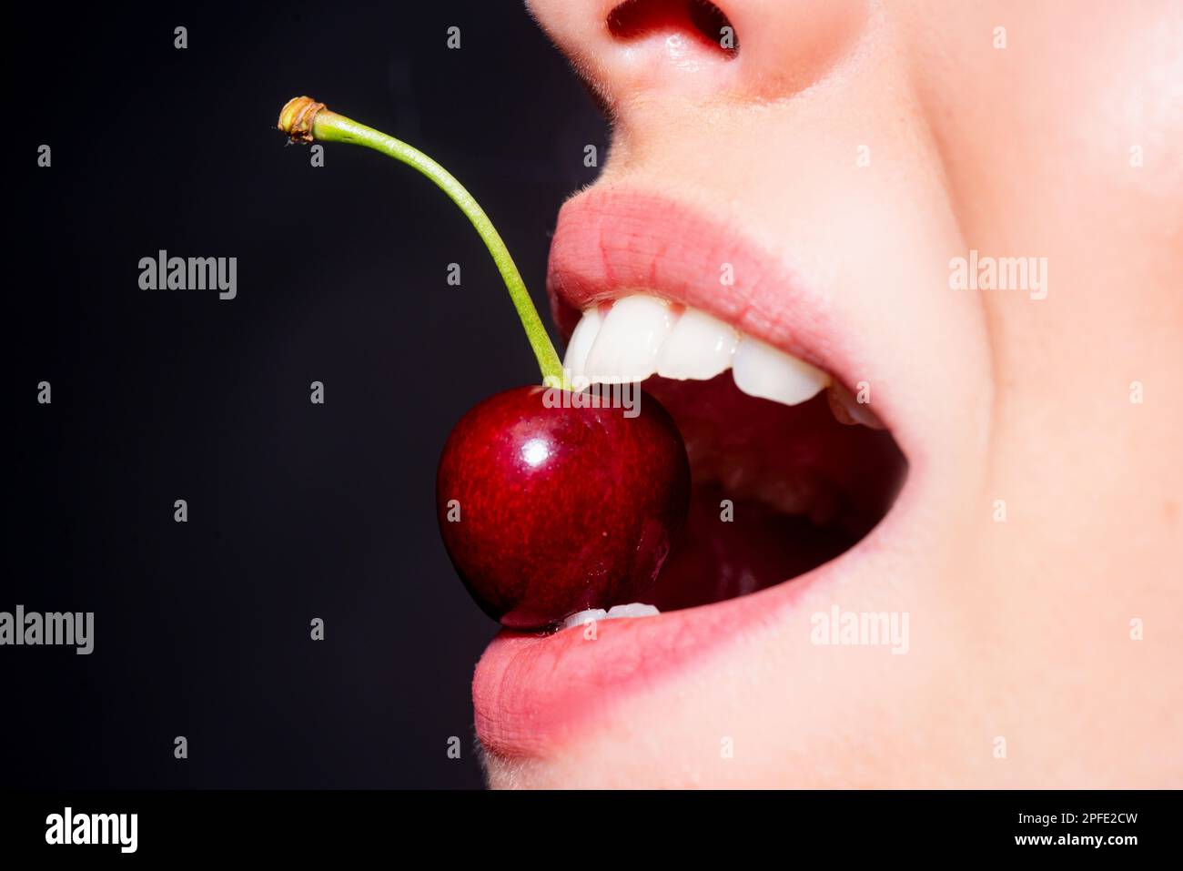 Cherry in teeth, macro, close up. Cherry in woman mouth. Beautiful girl ...
