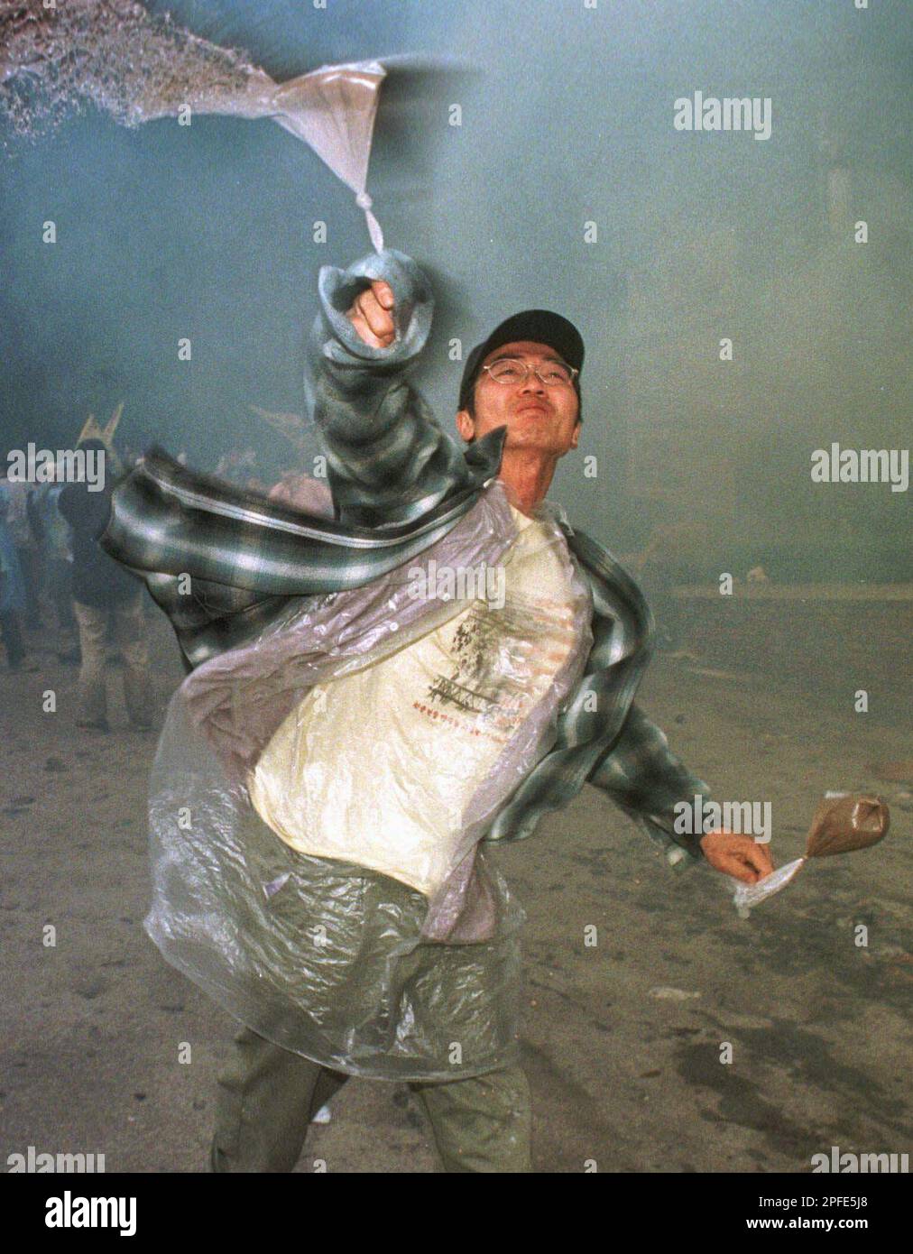 A student hurls a plastic bag containing paint at police under the rain ...