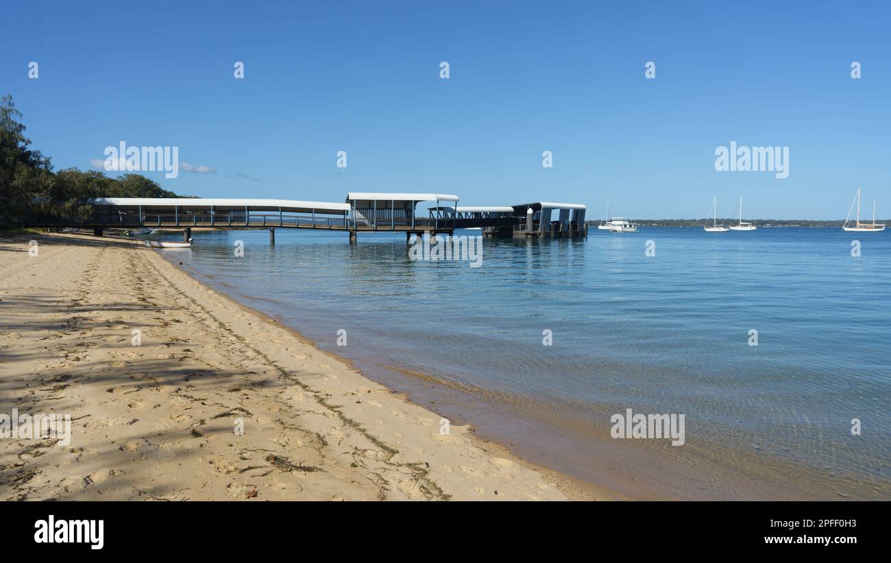 View along Main Beach on Coochiemudlo Island past the jetty, two boats on the tranquil water of ...