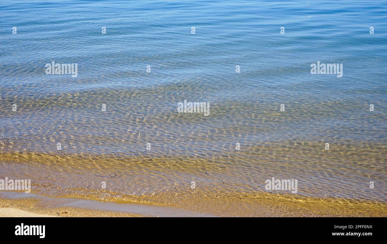 Dappled light in calm, clear water as it washes ashore on a sandy beach ...