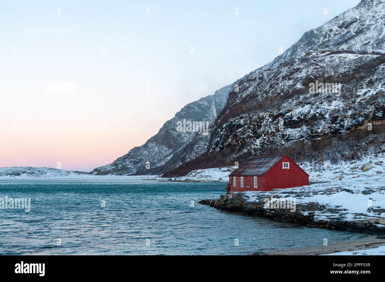 A traditional norwegian red barn enclosed by rugged mountains and snow ...