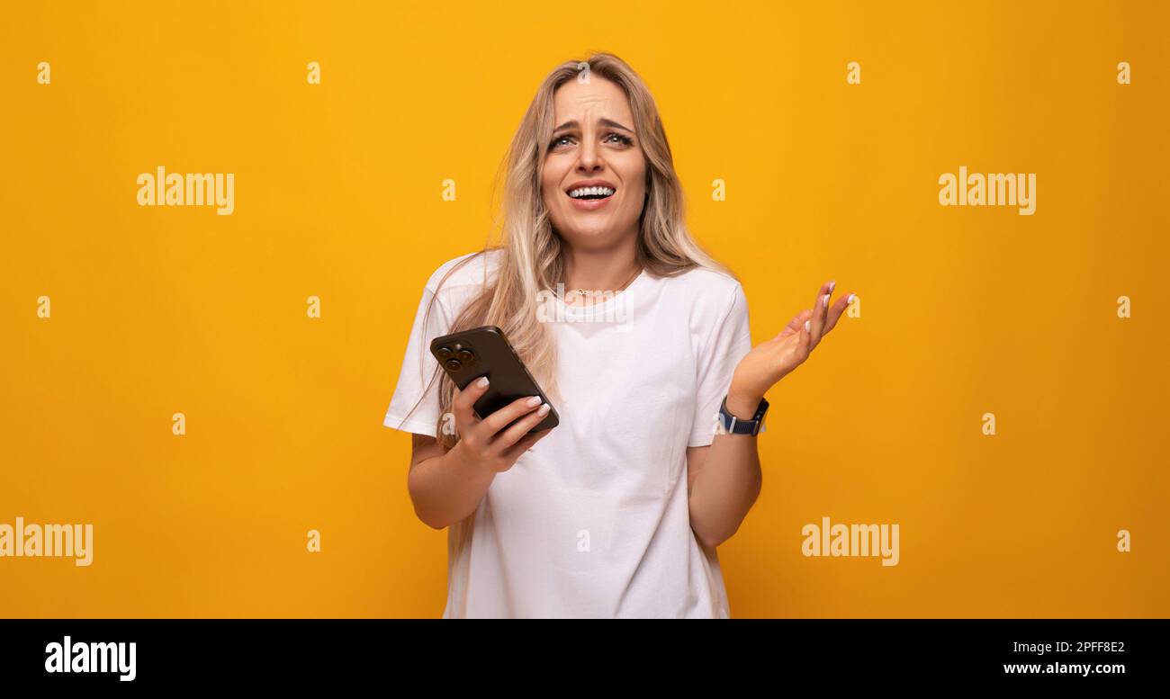 indignant girl holding a smartphone in her hands on a yellow background ...