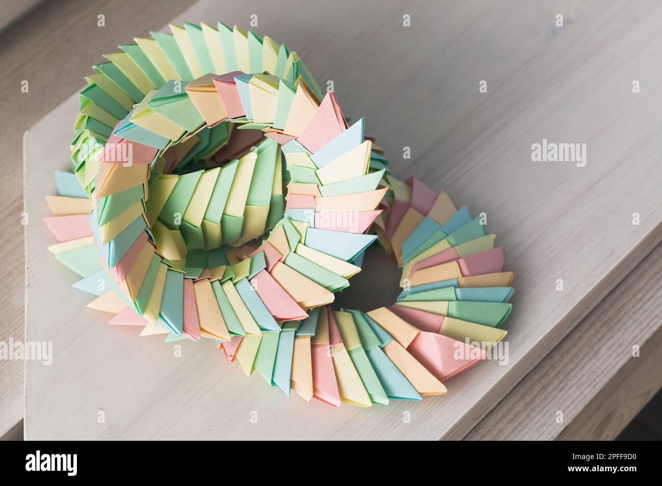 Origami rings made of colorful paper lay on a white wooden table ...