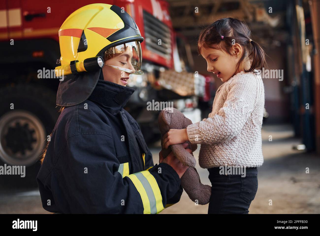 Happy little girl is with female firefighter in protective uniform ...