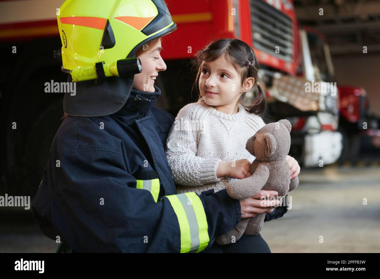 Happy little girl is with female firefighter in protective uniform ...