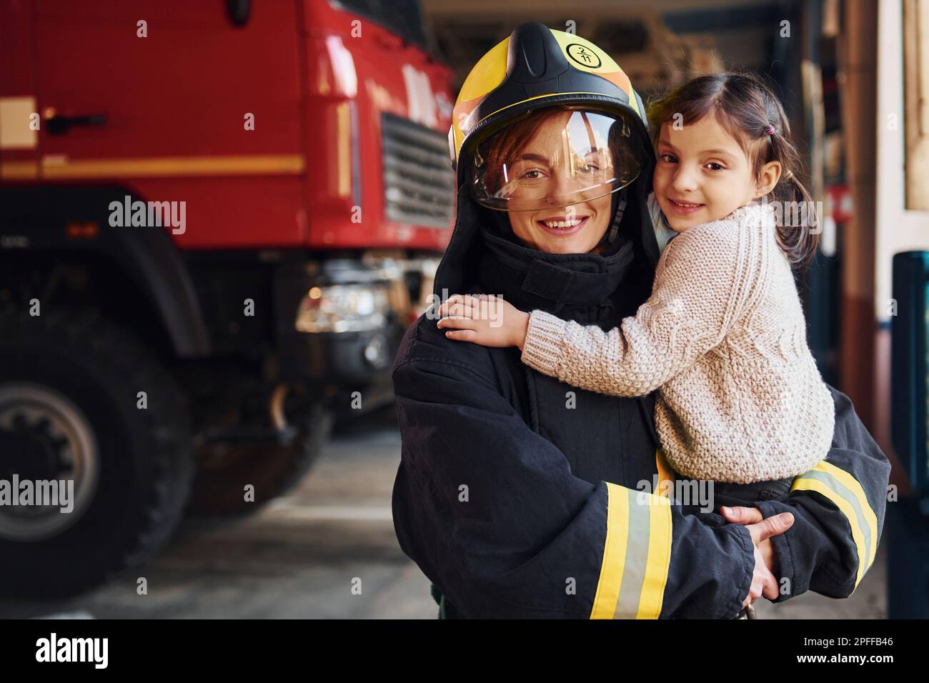 Happy little girl is with female firefighter in protective uniform ...