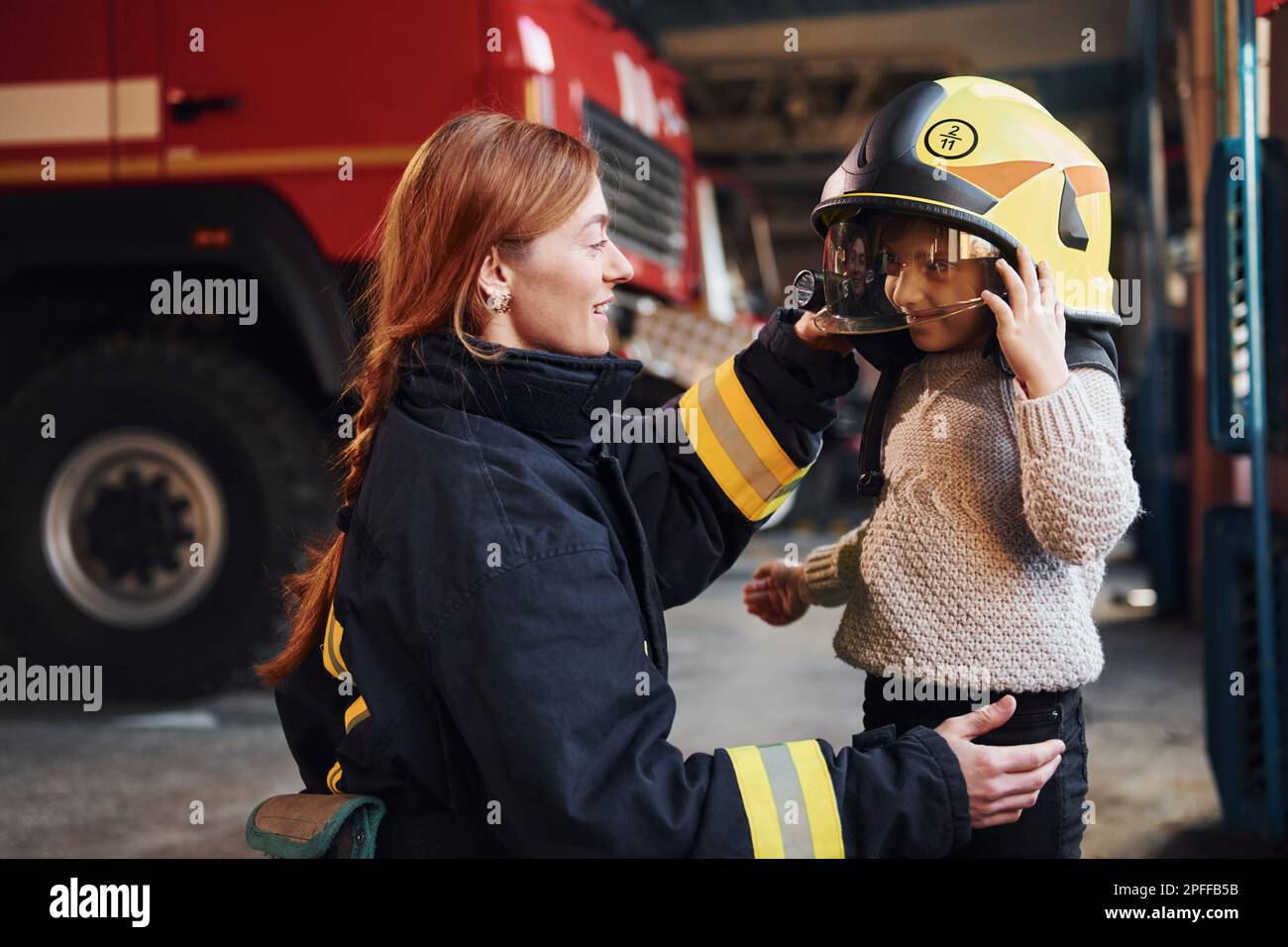 Happy little girl is with female firefighter in protective uniform ...