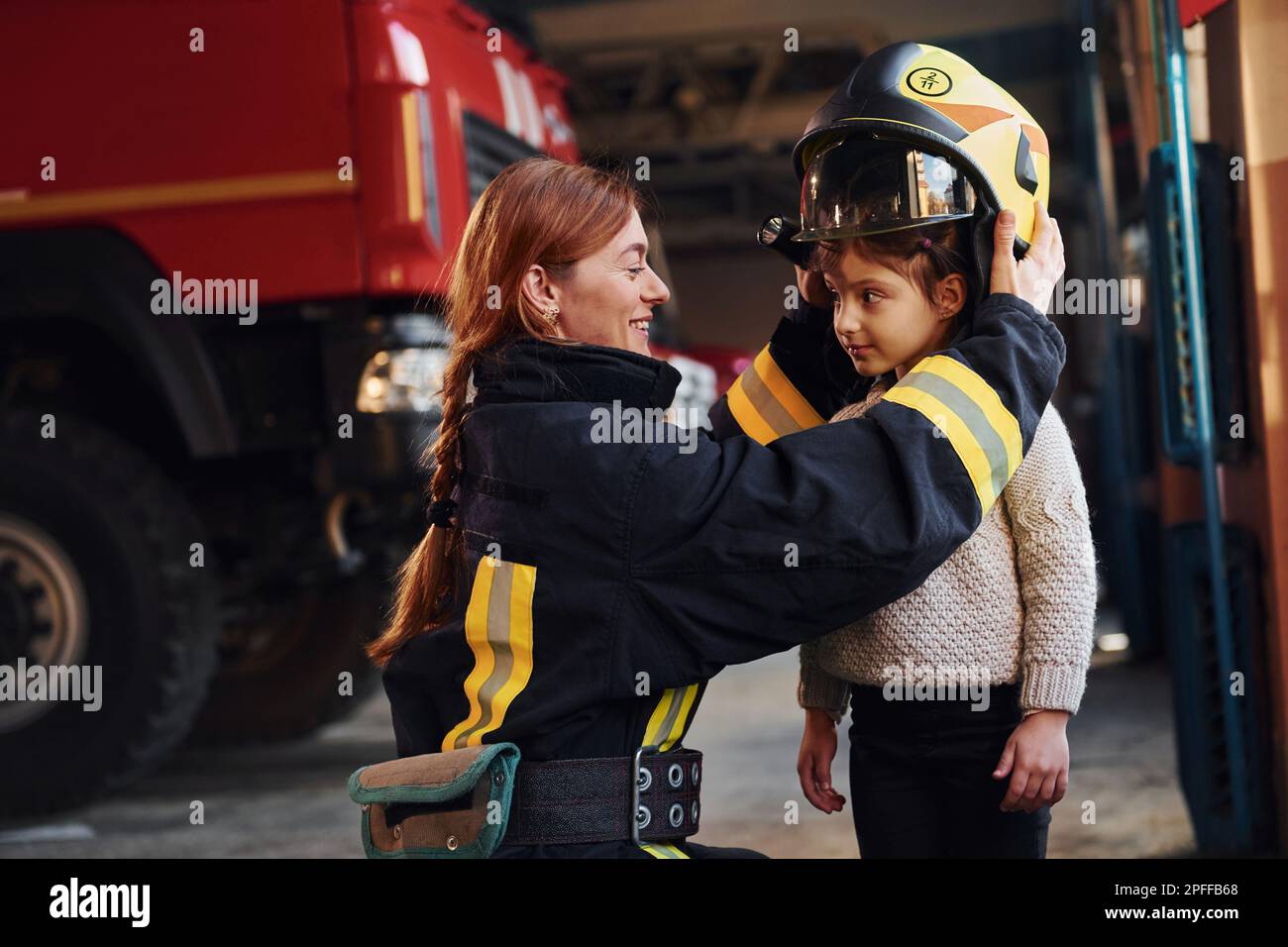 Happy little girl is with female firefighter in protective uniform ...