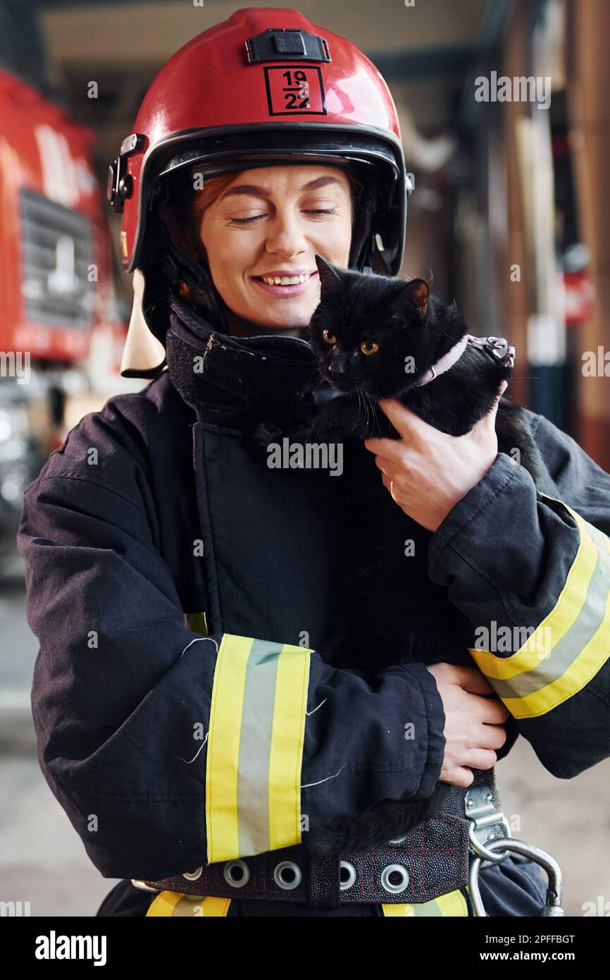 Cute black cat. Female firefighter in protective uniform standing near ...