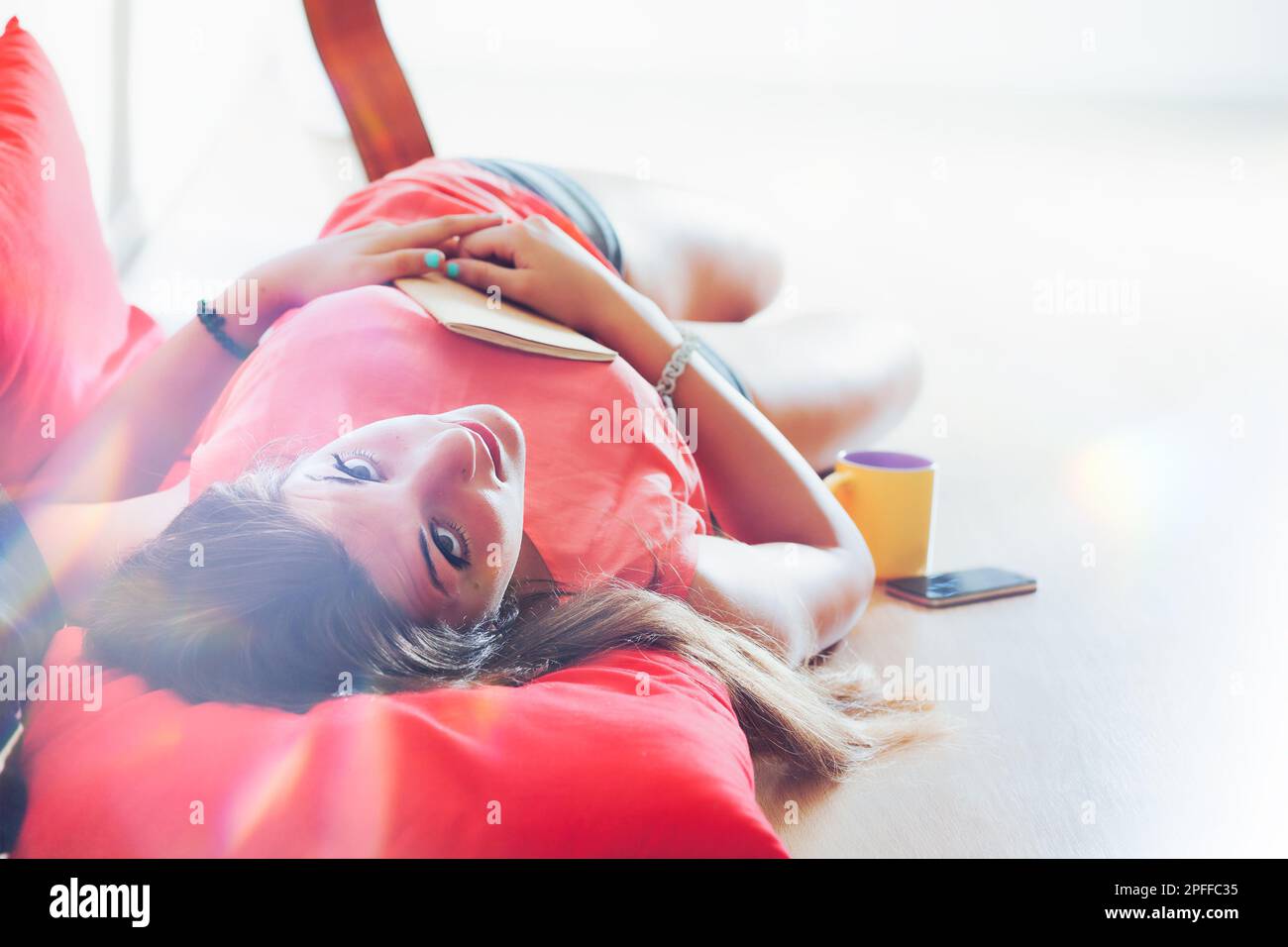 Reversed shot of young woman lying with a notebook on her belly and ...