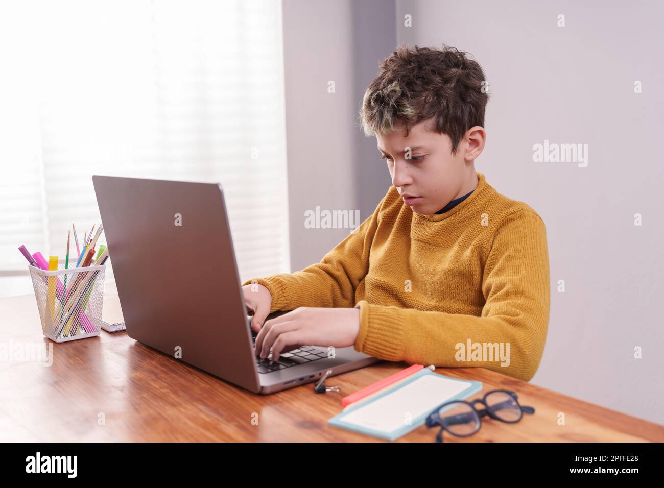 A side view of a young boy sitting at a desk and typing on a laptop ...