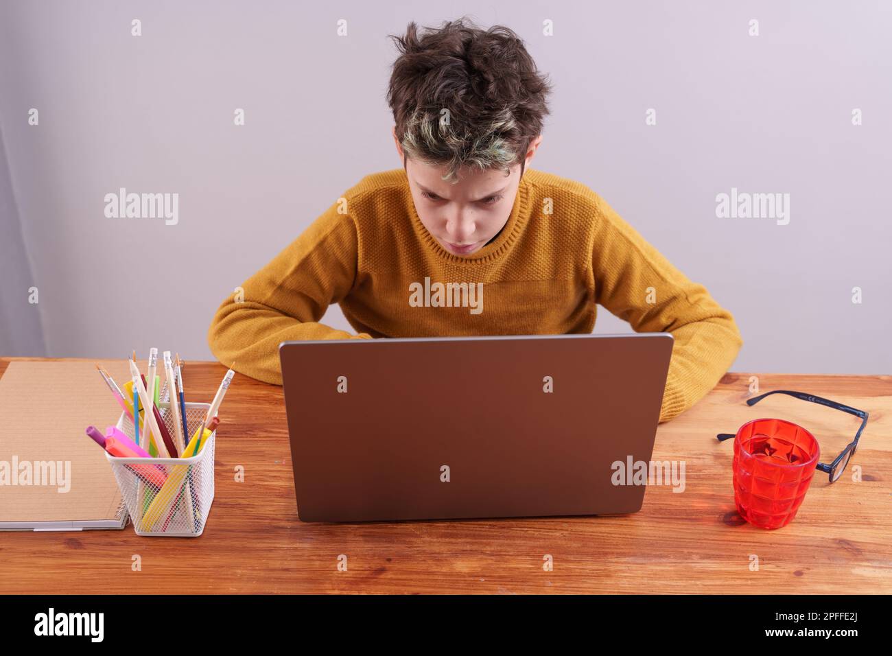 A focused 10-year-old boy is typing on a laptop keyboard with his hands ...