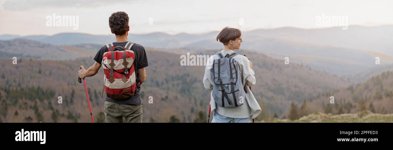 Back view on male and female hikers with walking sticks on top of ...