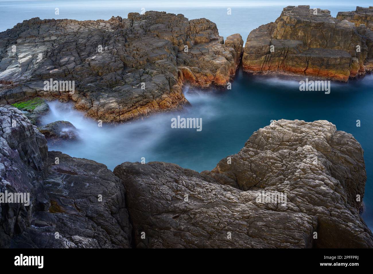Landscape of blue sea, mountains and textured rocks. Hazy dreamy sky ...
