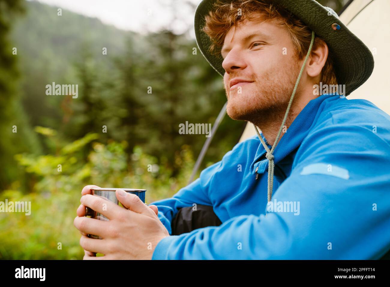 Young ginger man wearing panama drinking hot tea while sitting at ...