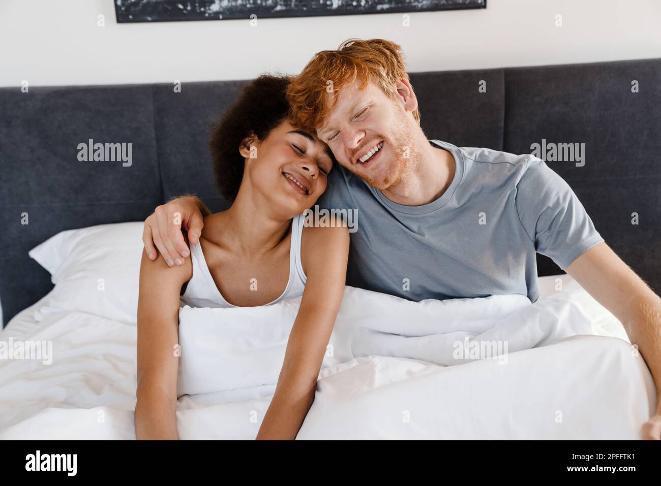 Young beautiful smiling interracial couple with closed eyes hugging ...