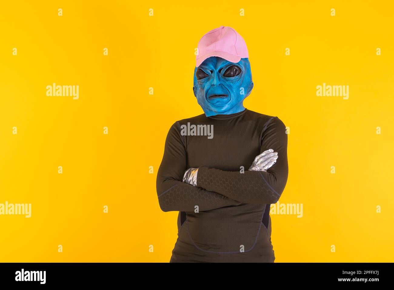 Man with blue headed alien mask, wearing a pink cap, arms crossed ...