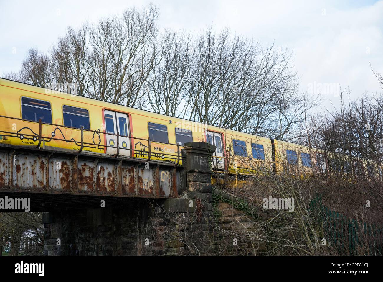 Merseyrail train arriving at Maghull rail station. Crossing an old iron ...