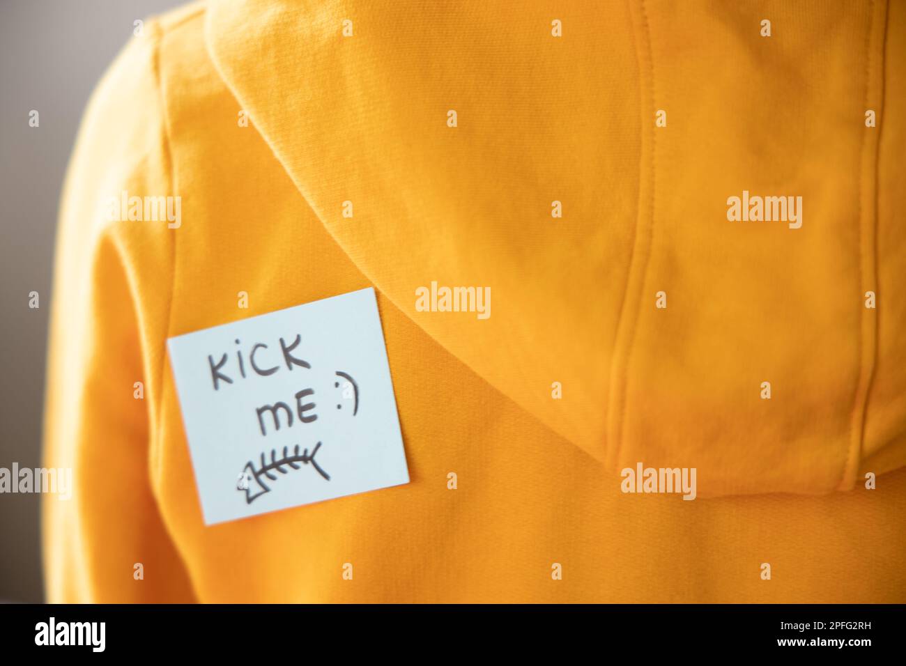 Boy in yellow hoodie with a sticky note on his back, saying kick me ...