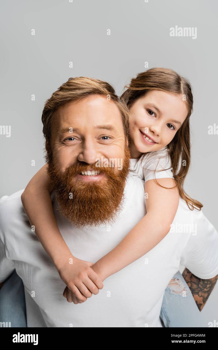 Overjoyed preteen girl piggybacking on bearded dad isolated on grey ...