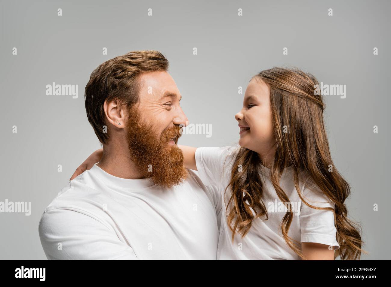 Side view of smiling girl in white t-shirt hugging bearded dad isolated ...