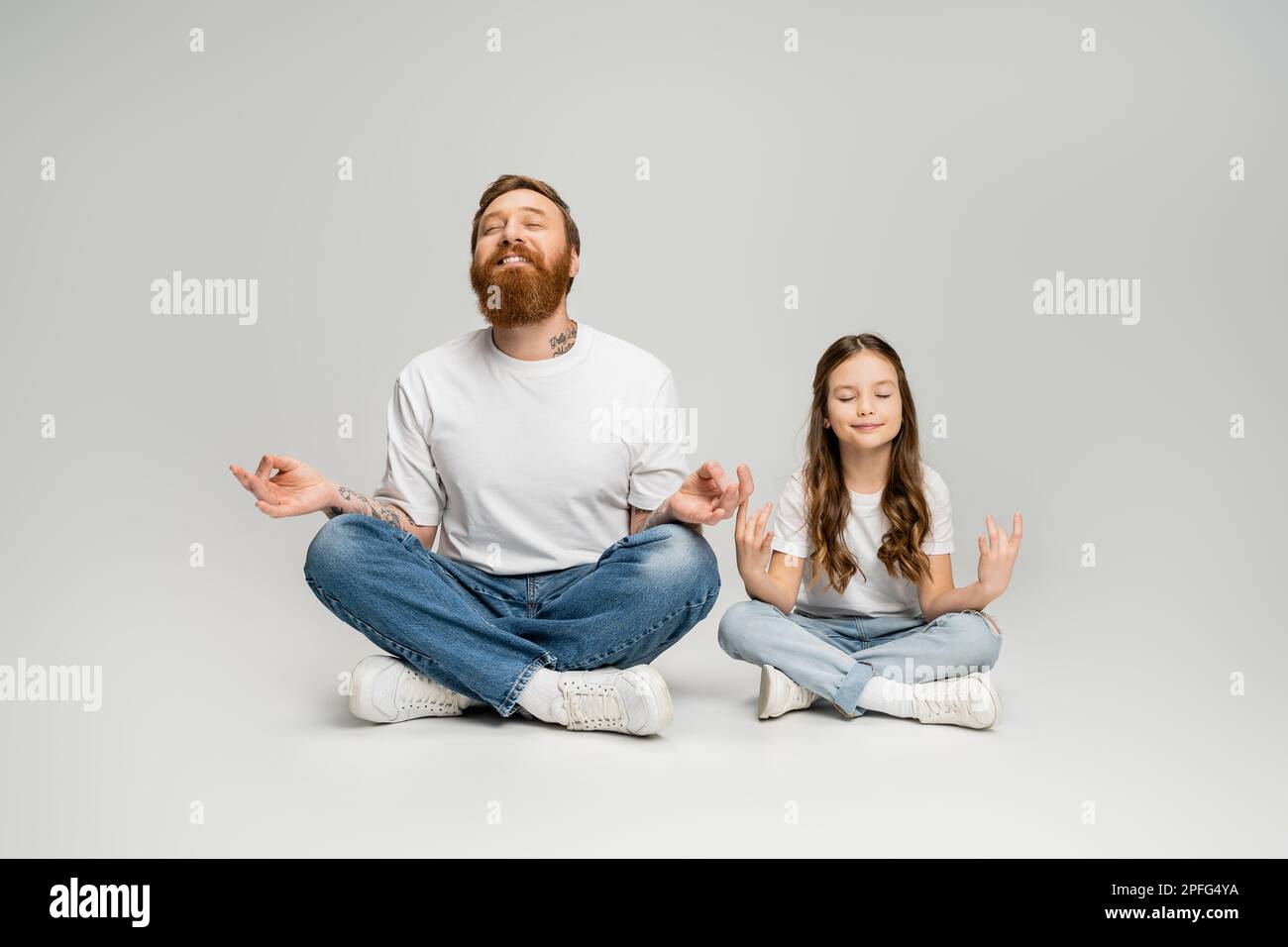 Smiling man and daughter doing gyan mudra while meditating on grey ...