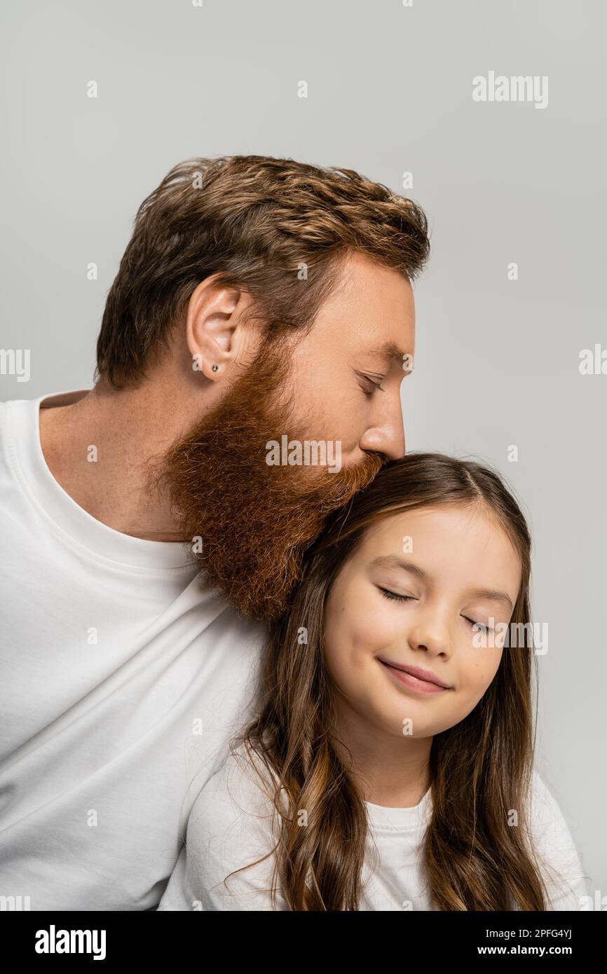 Bearded dad kissing head of smiling preteen daughter with closed eyes ...
