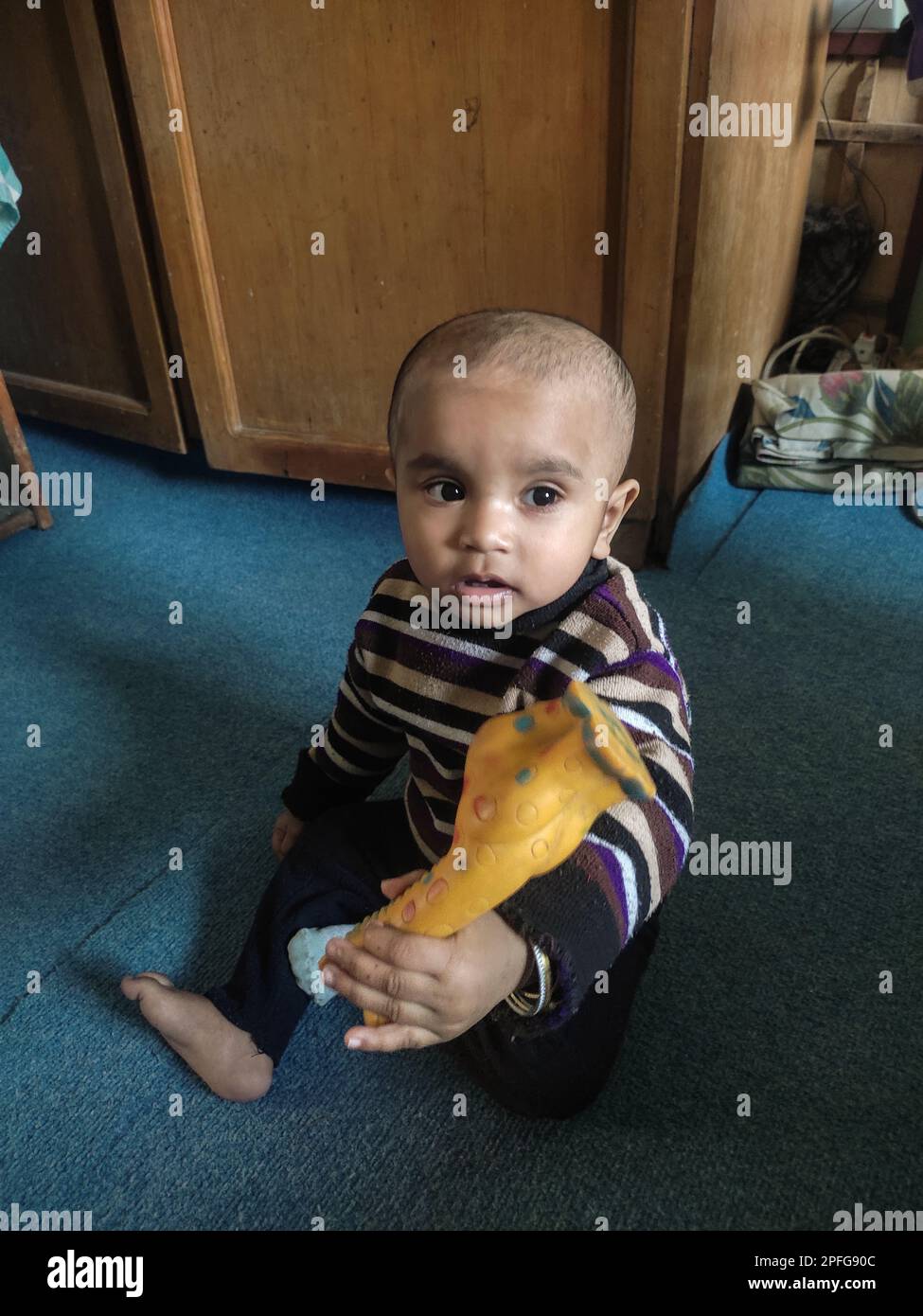 Asian cute baby sitting and playing a small toy on soft mat at home ...