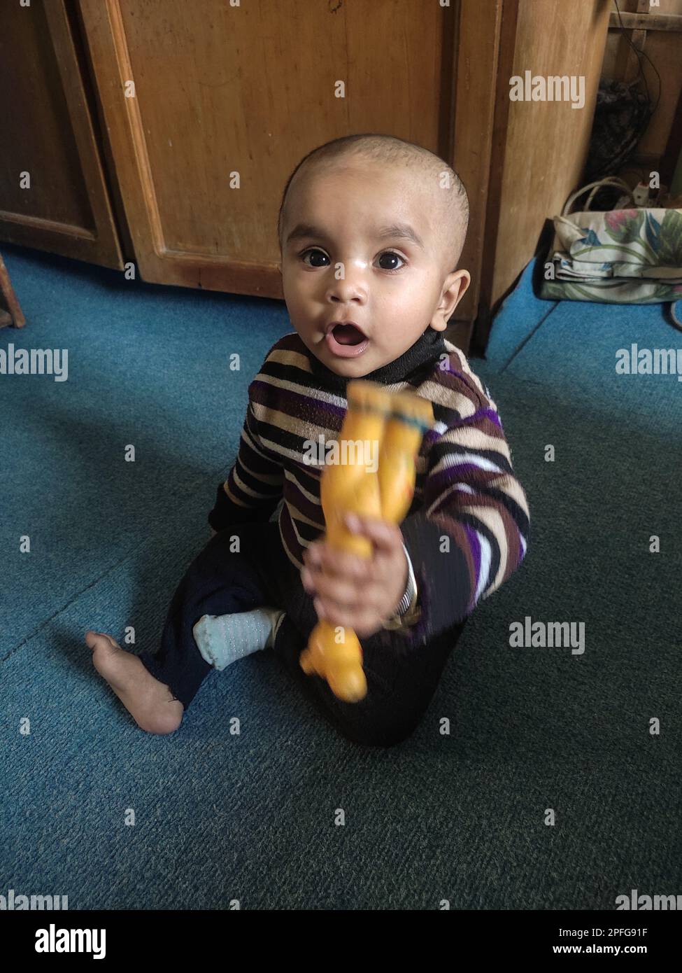 Asian cute baby sitting and playing a small toy on soft mat at home ...