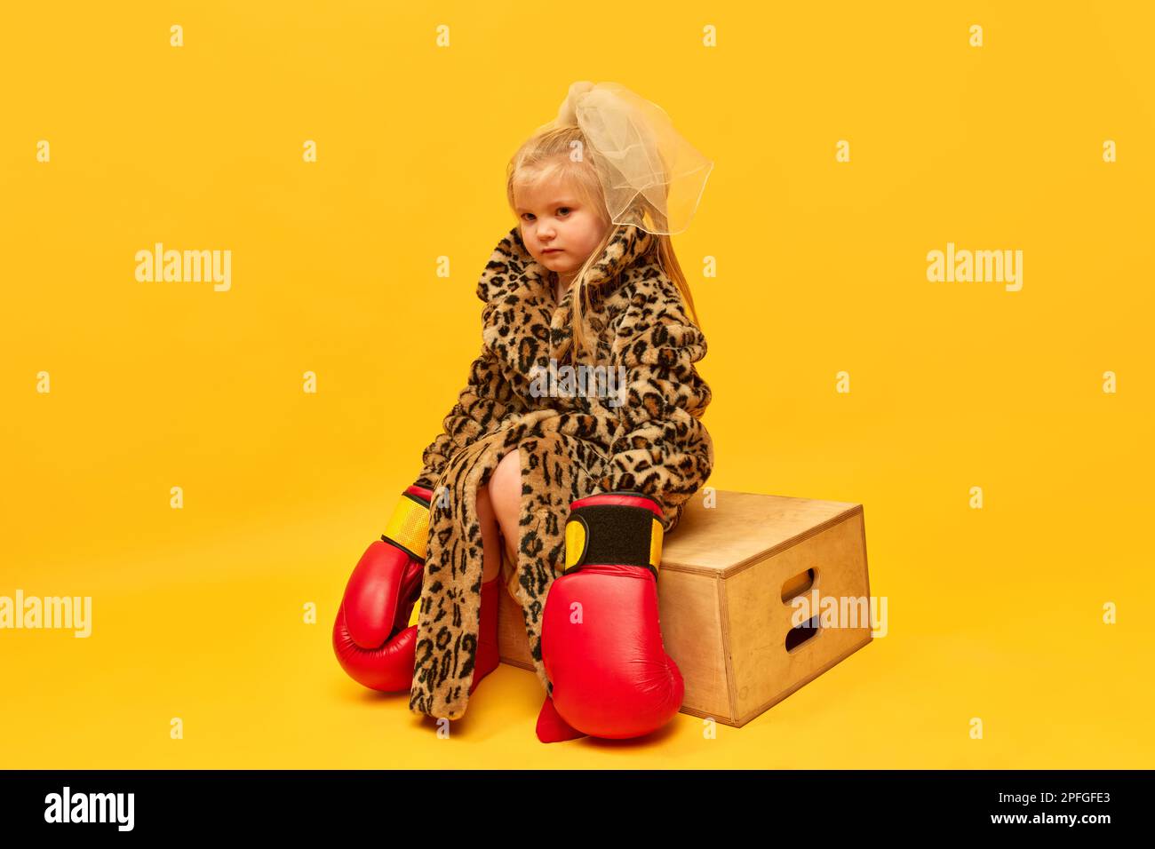 Little upset blond girl wearing boxing gloves and leopard coat sitting ...
