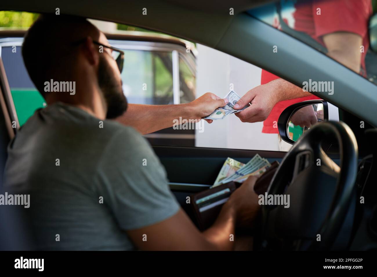 Young man giving money to petrol station operator for refueling car ...