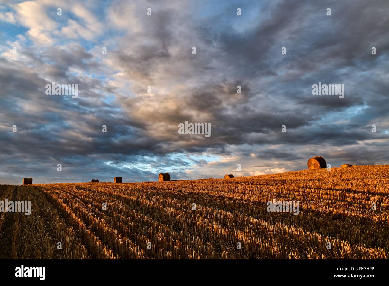 Cloudy sky over a field with bales of straw Stock Photo - Alamy