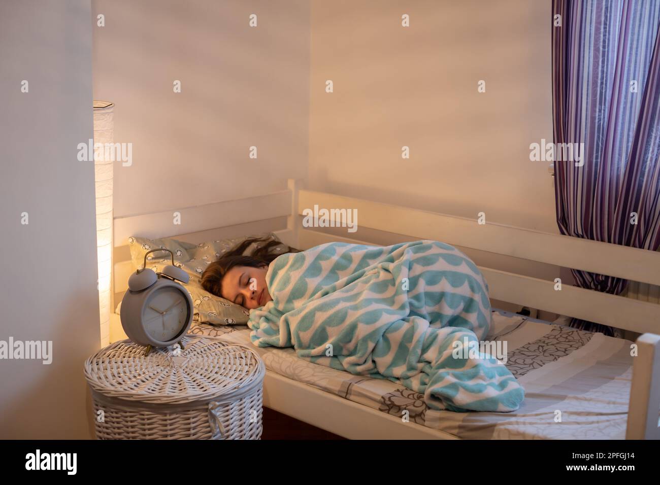 A curled-up woman lies on her bed wrapped in a blue blanket Stock Photo ...