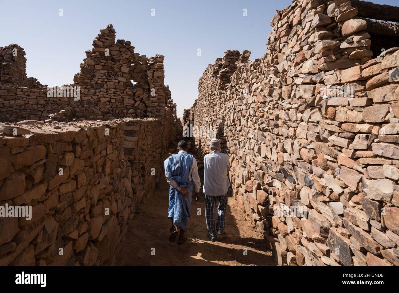 Two locals in traditional clothing walk amidst the weathered ruins of ...