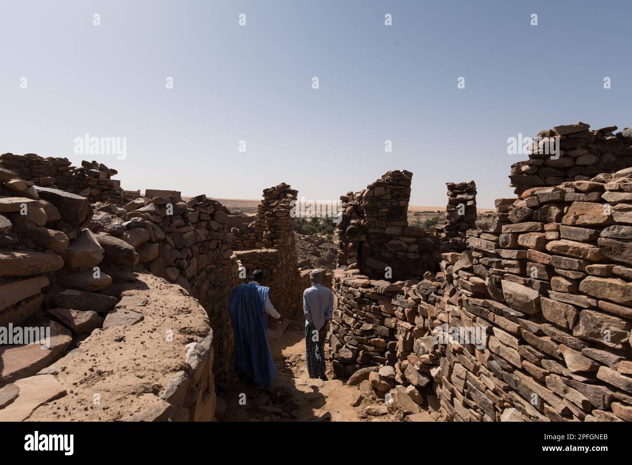 Two locals in traditional clothing walk amidst the weathered ruins of ...