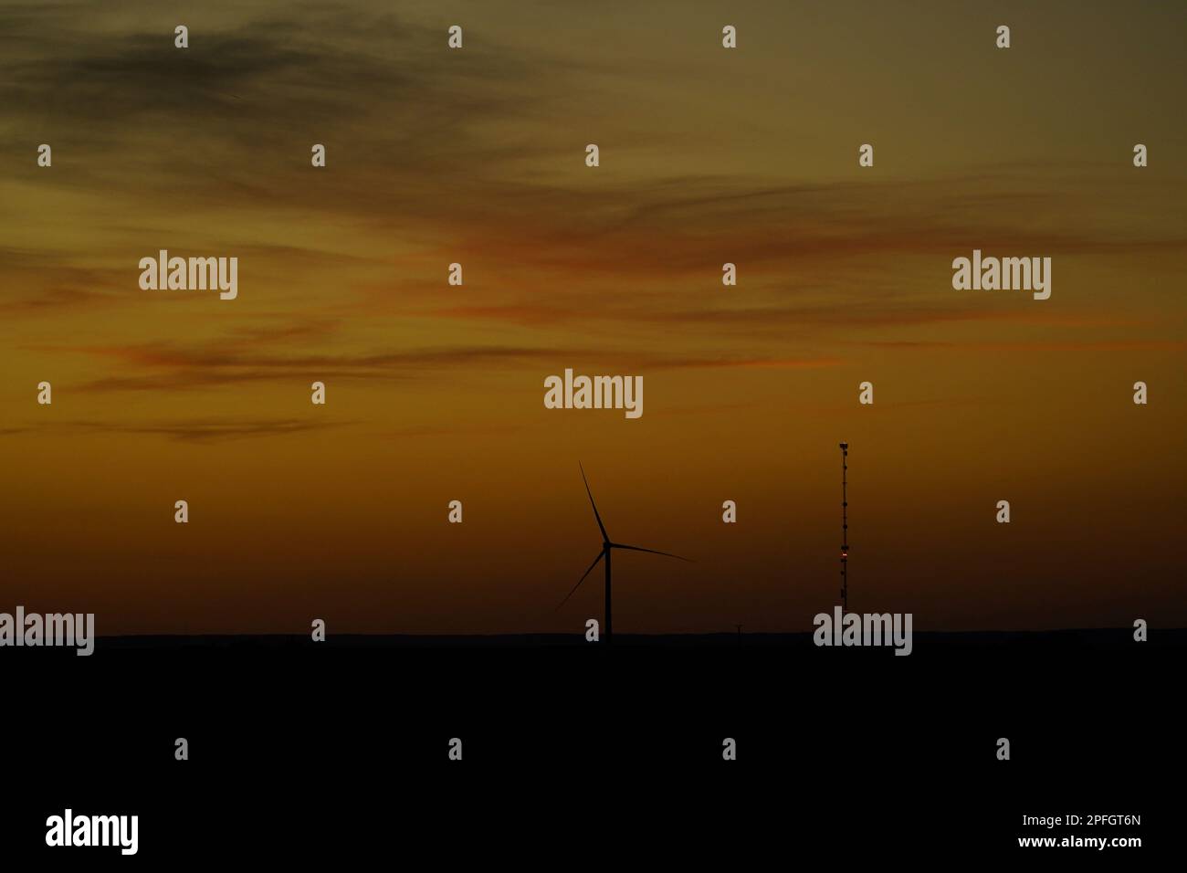 A wind turbine and communications tower are seen at sunset of a wind ...