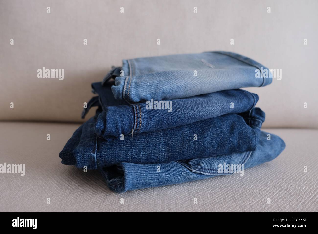 Denim pants, four folded and stacked denim pants on a white sofa, denim ...