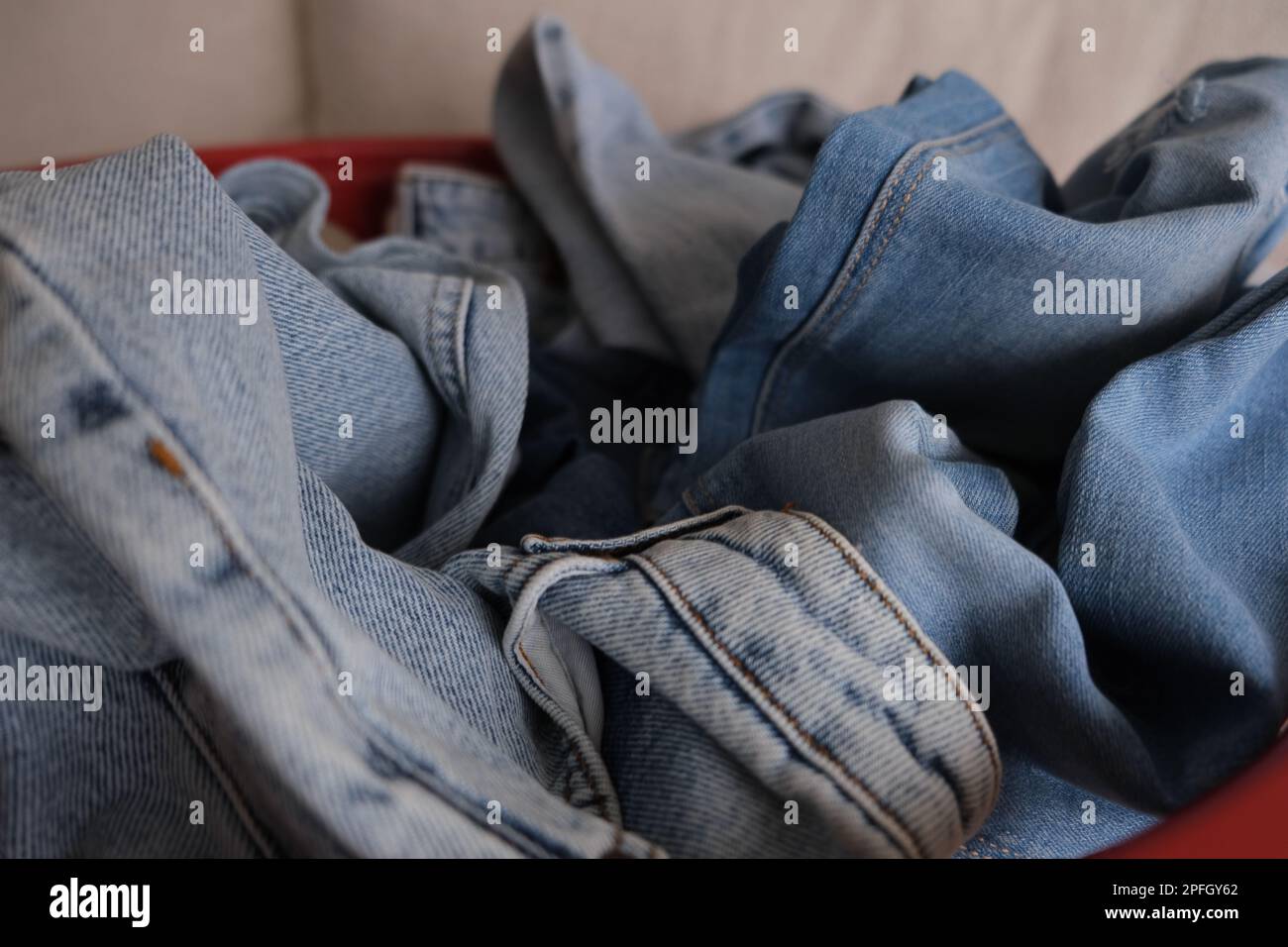 Crumpled denim pants, unfolded denim pants in a red basket on a white ...