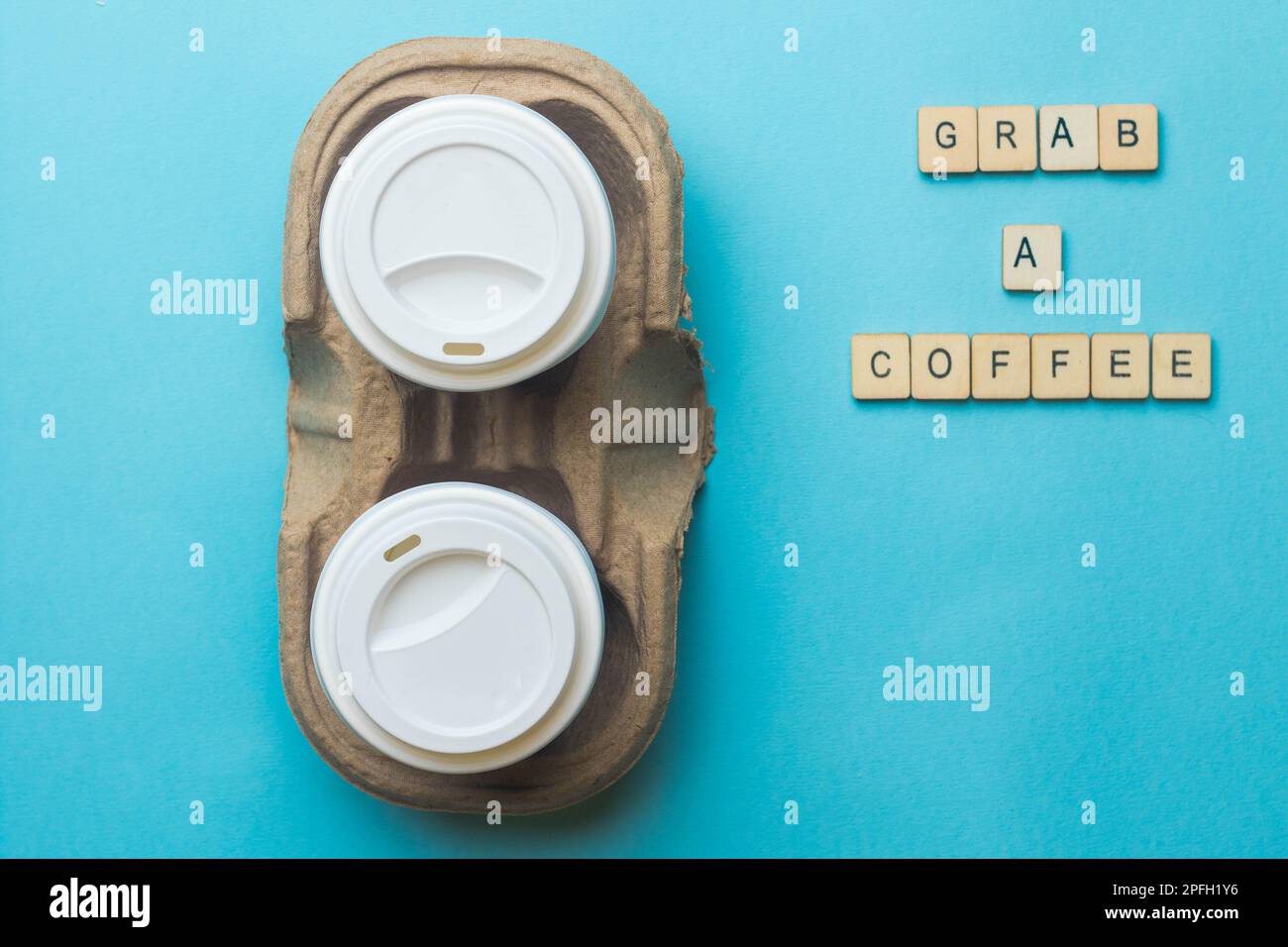 A cardboard tray with 2 coffee cups and lids with a sign reading grab a ...